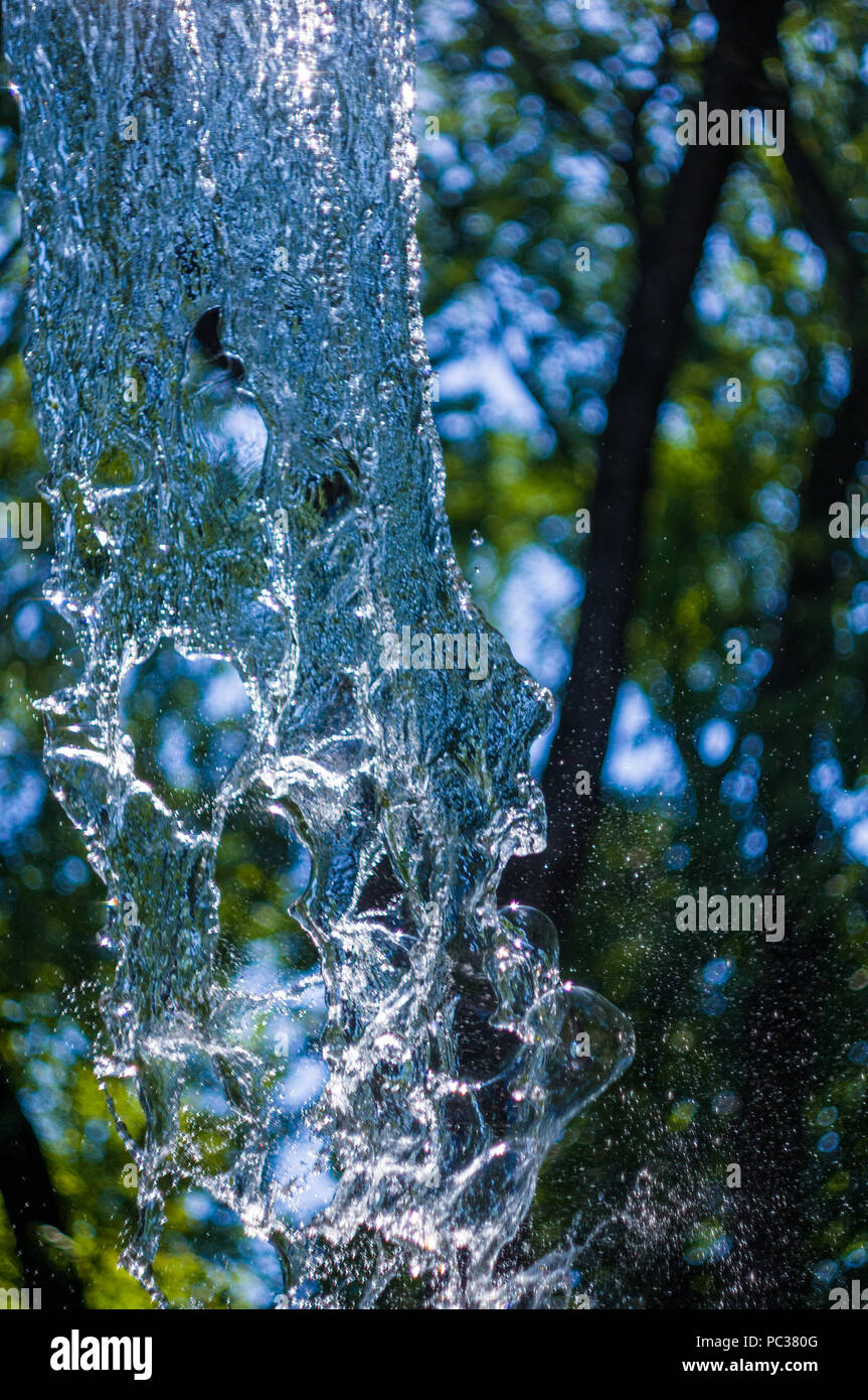 transparent falling water vertical flows against a blue sky and green ...