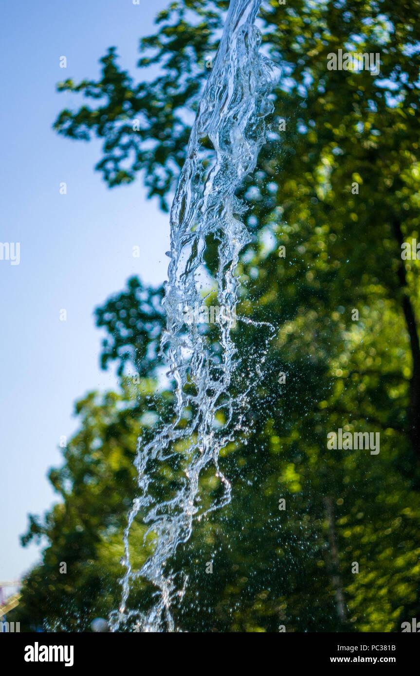 transparent falling water vertical flows against a blue sky and green ...