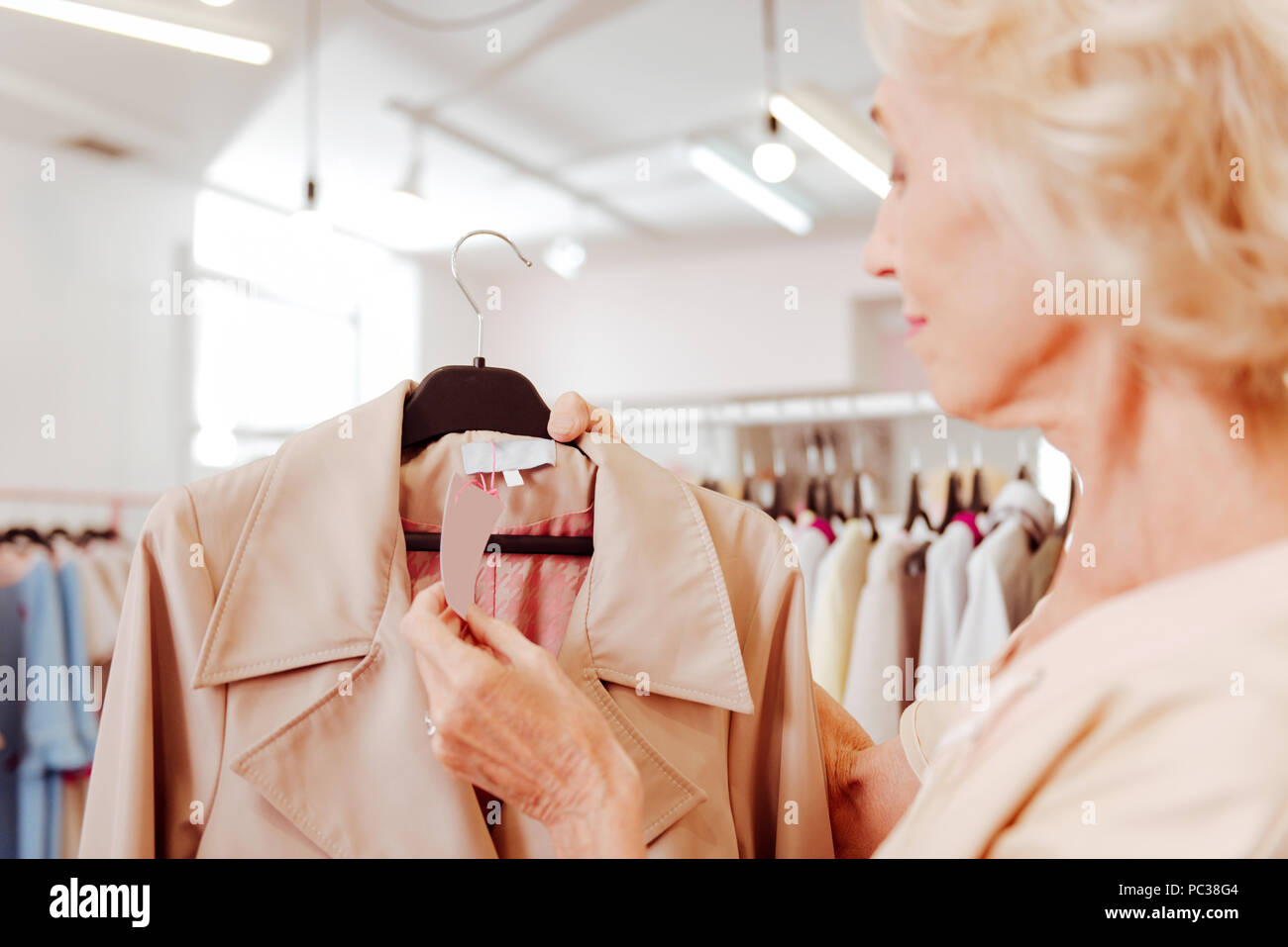 Buying coat. Stylish woman holding price tag of coat while shopping on ...