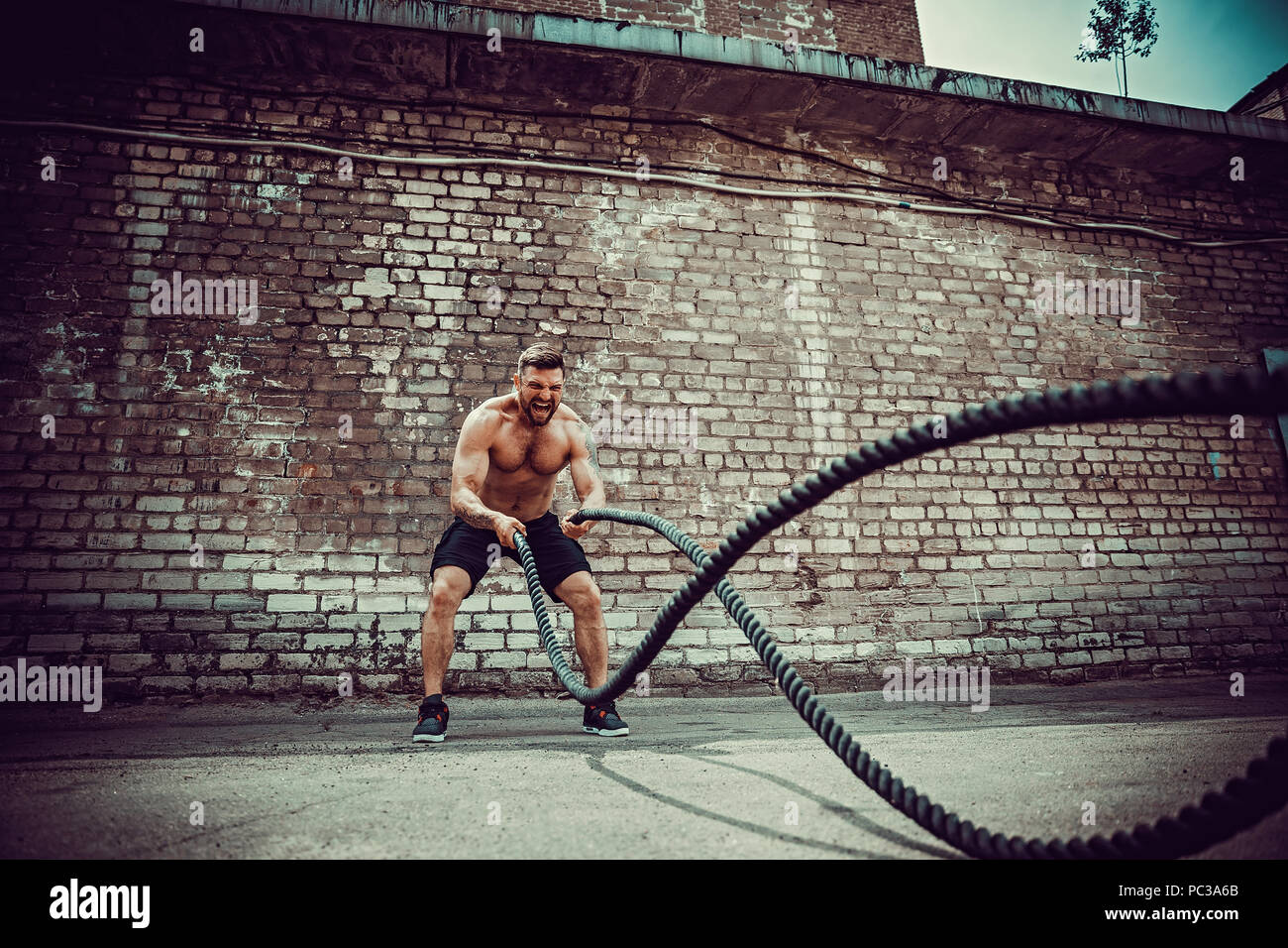 Athletic man working out with rope in front of brick wall. Strength and ...