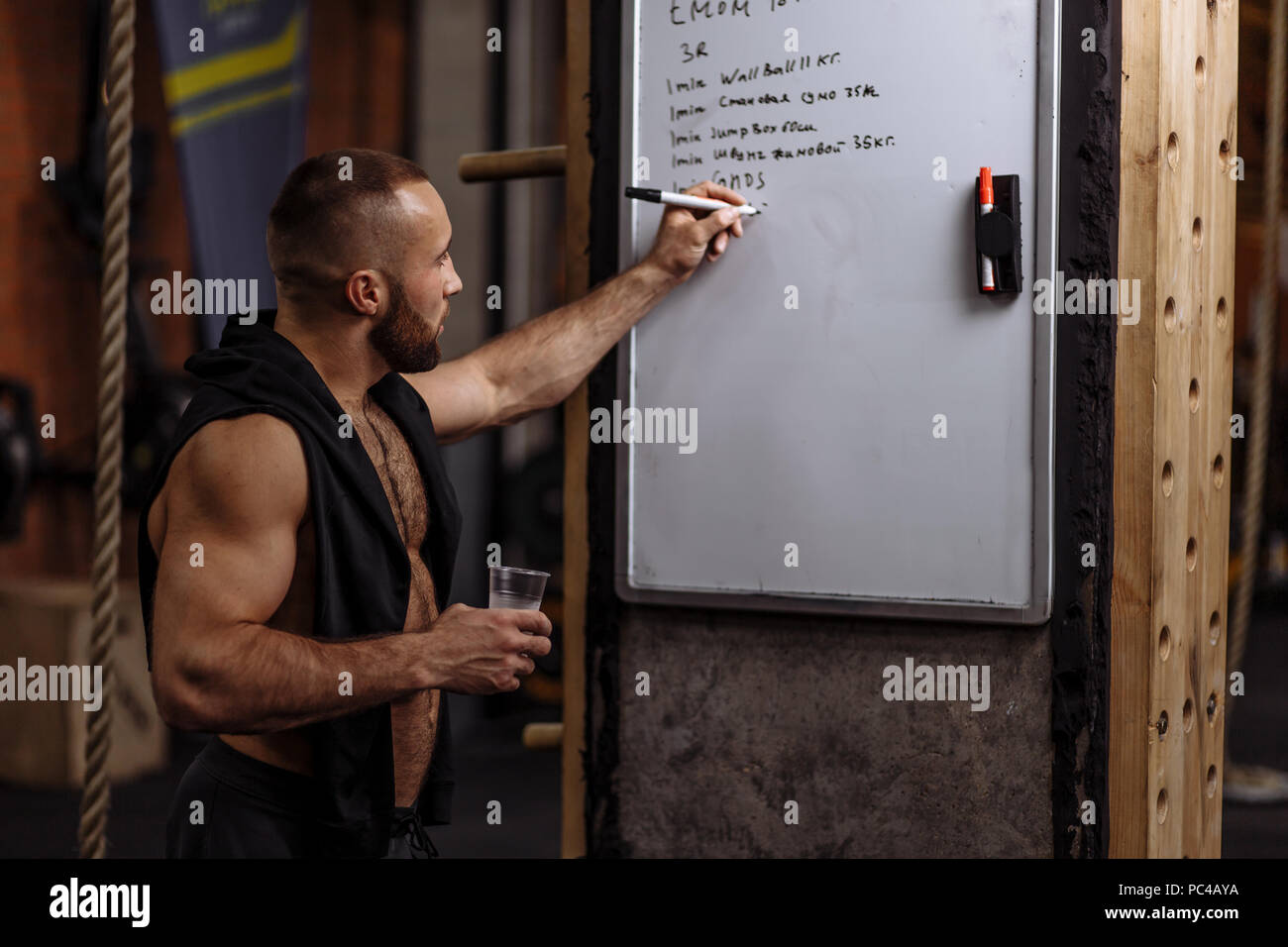 pleasant muscular man is writing workout routine on the flipchart while ...