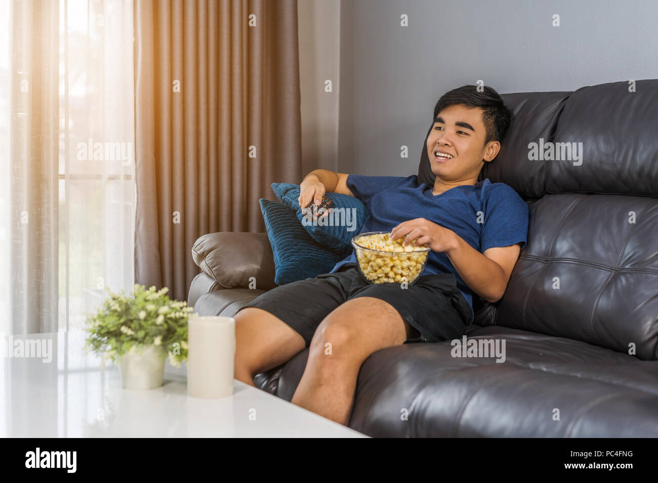young man eating popcorn while sitting on a couch at home and watching ...