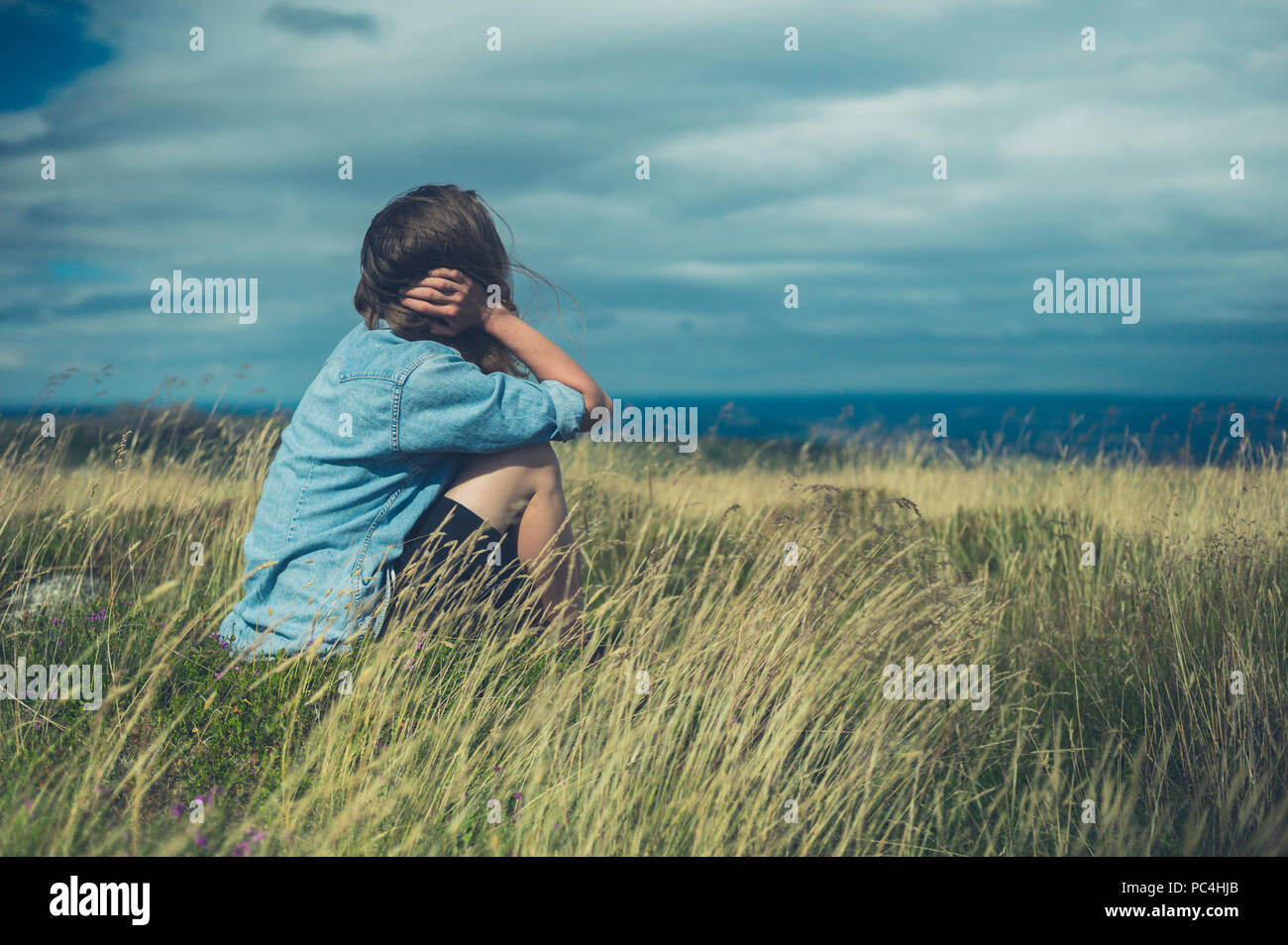 A sad woman is sitting in a field on a windy day Stock Photo - Alamy
