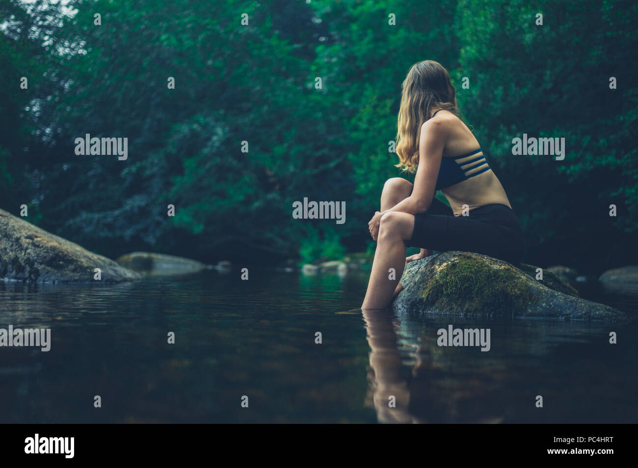 A young woman is sitting on a rock relaxing in the river Stock Photo ...