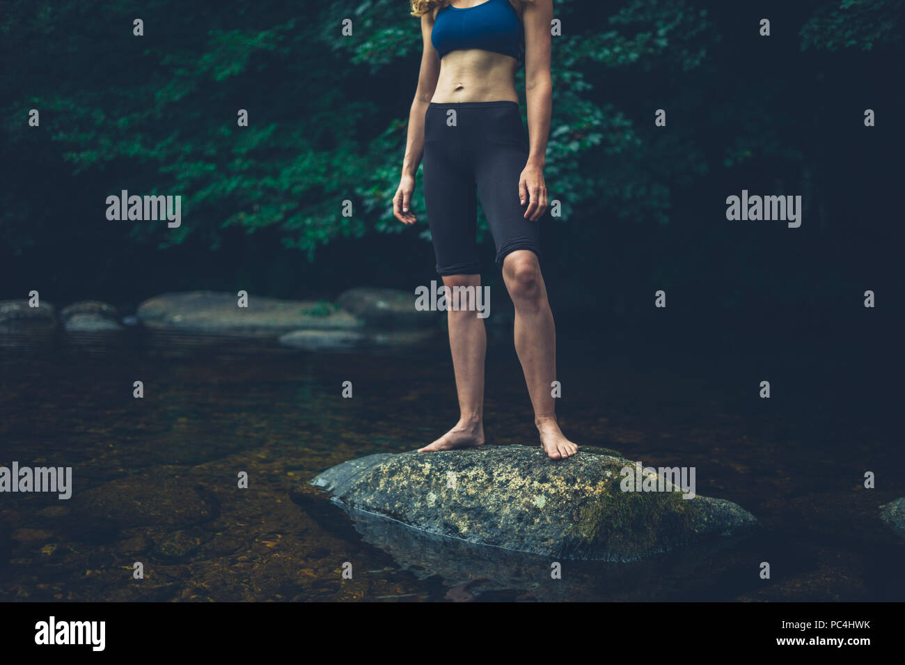 A young fitness woman is standing on a rock in the river Stock Photo ...