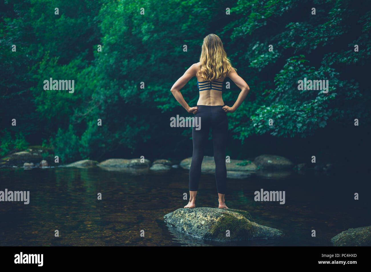 A young fitness woman is standing on a rock in the river Stock Photo ...