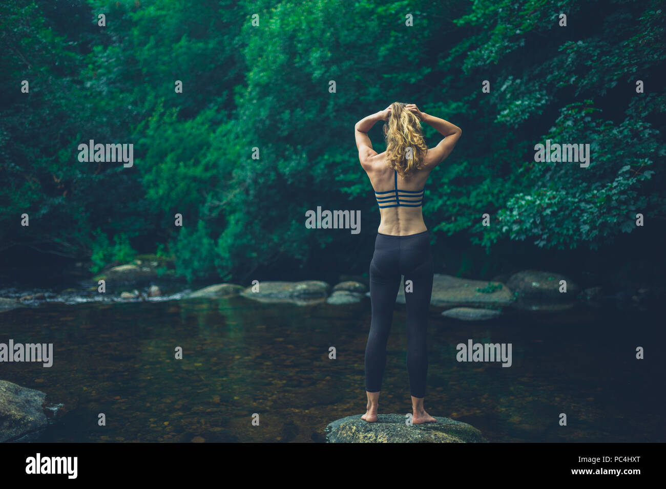 A young fitness woman is standing on a rock in the river Stock Photo ...