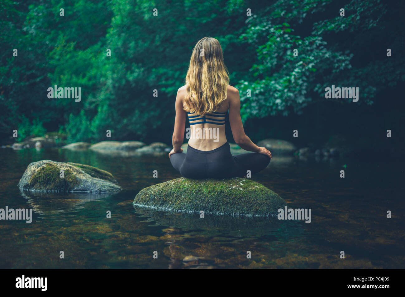A young woman is meditating on a rock in the river Stock Photo - Alamy
