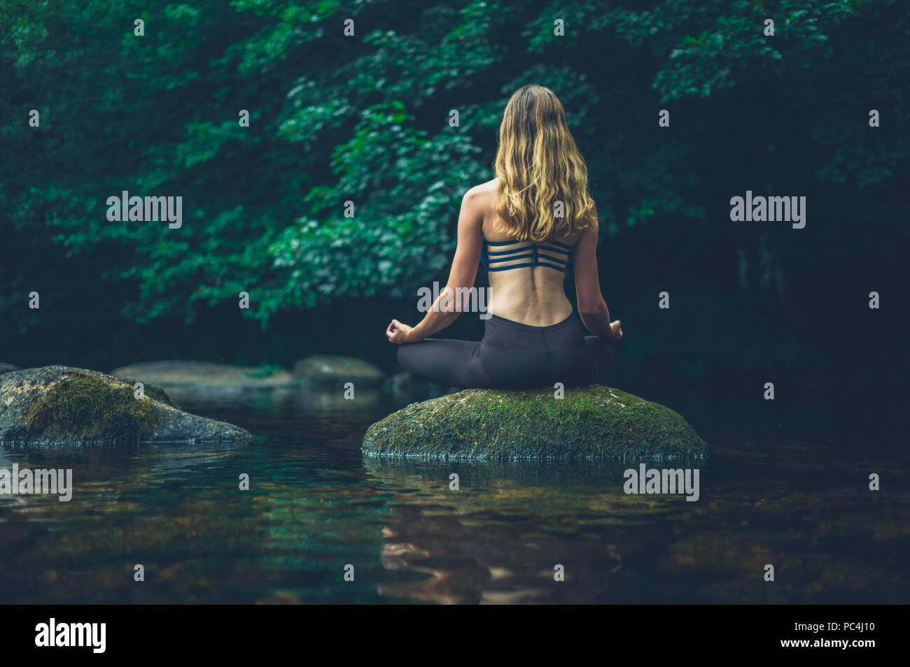 A young woman is meditating on a rock in the river Stock Photo - Alamy