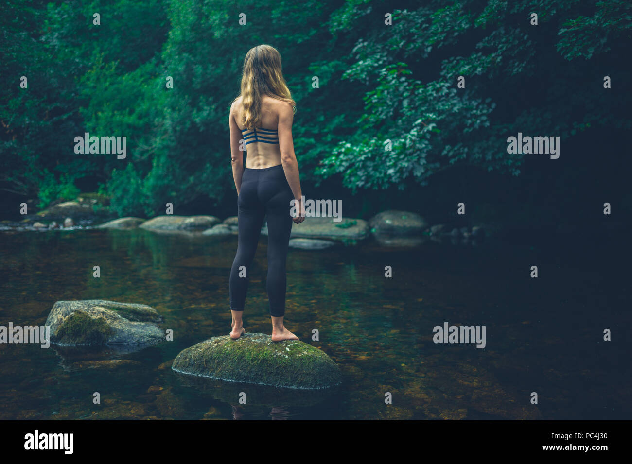 A young fitness woman is standing on a rock in the river Stock Photo ...