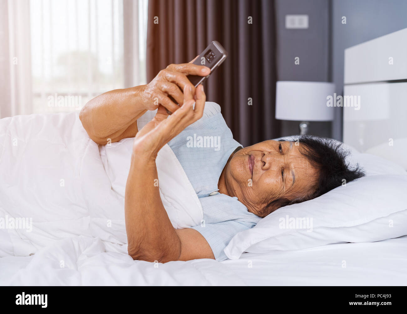 senior woman using mobile phone on a bed Stock Photo - Alamy