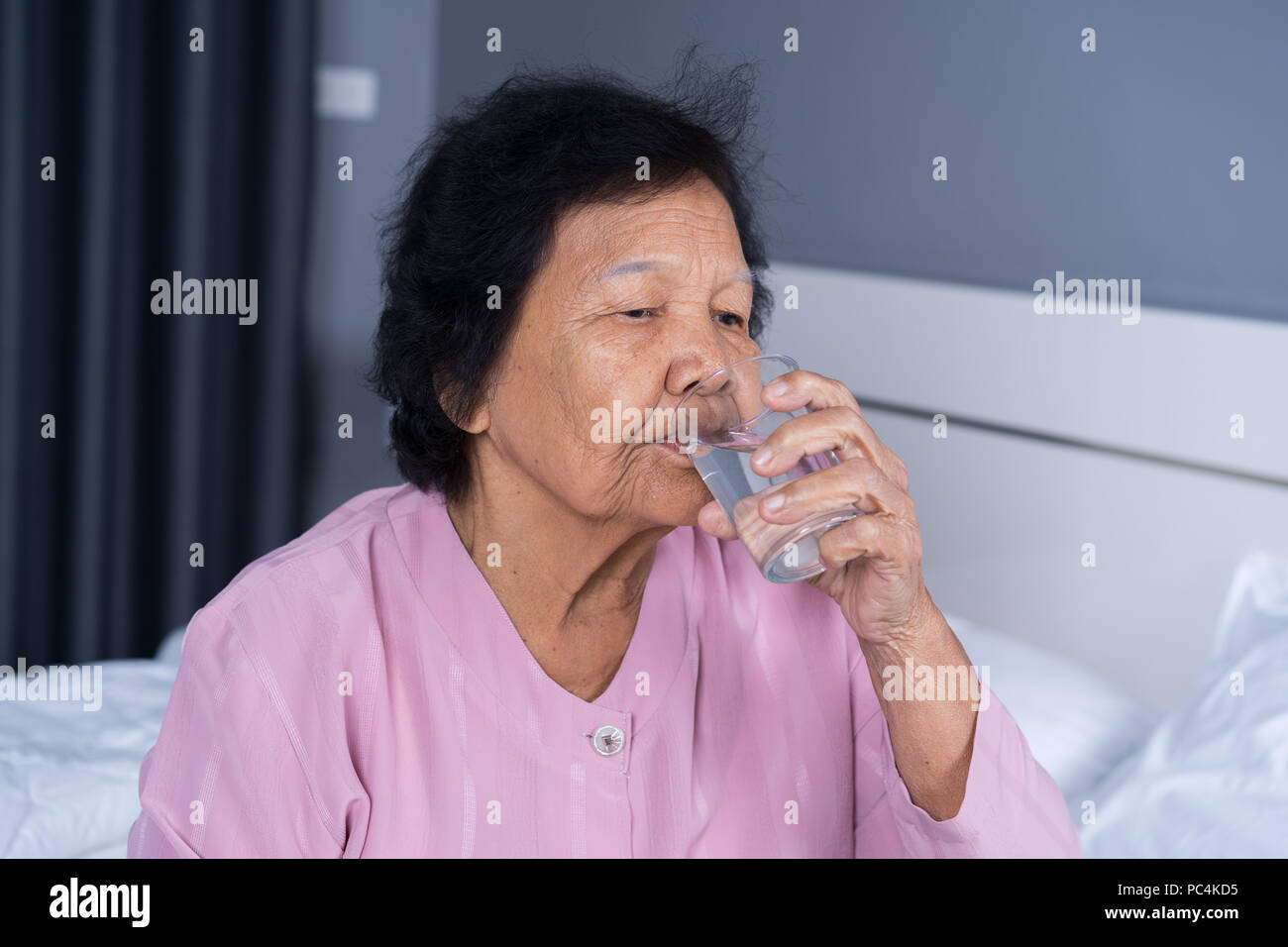 Senior woman drinking water in the bedroom Stock Photo - Alamy