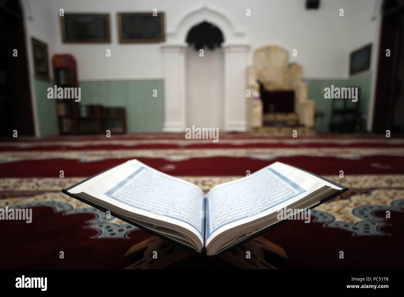 An open Holy Quran on wood stand with mihrab in background. | usage ...