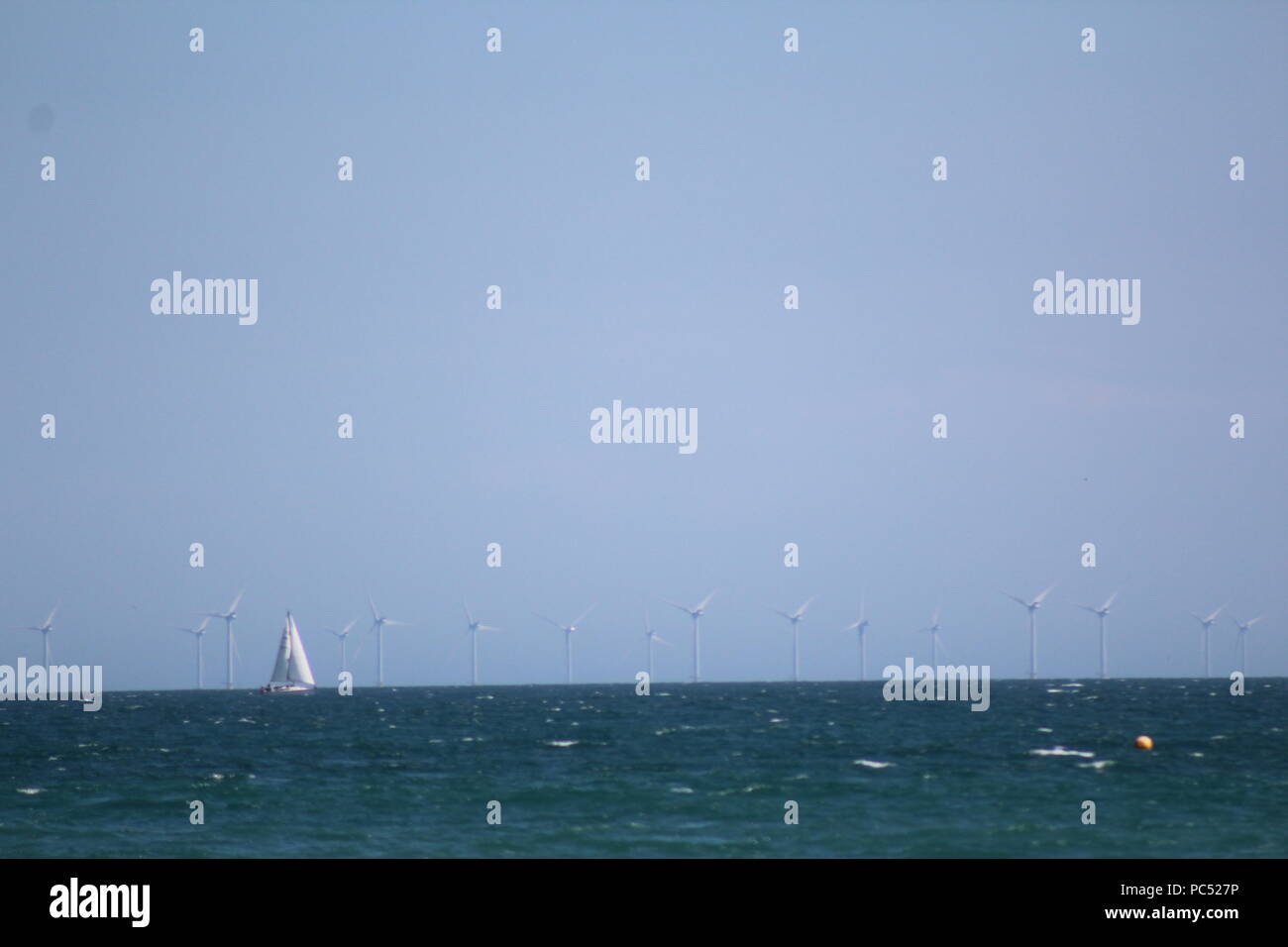 White sailing boat on the sea with off shore wind turbines on the ...