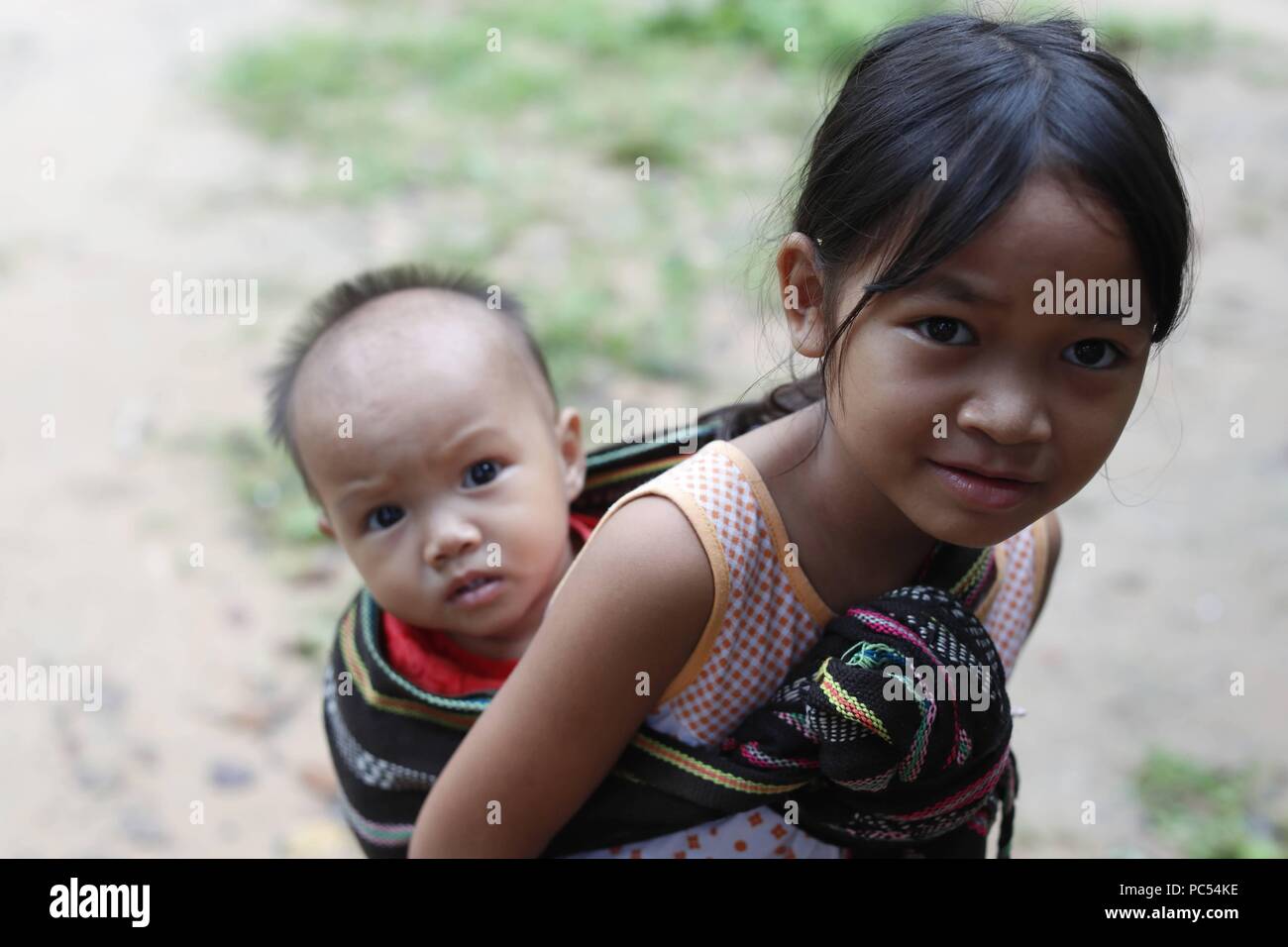Bahnar (Ba Na) ethnic group. Young girl carrying baby on her back. Kon ...