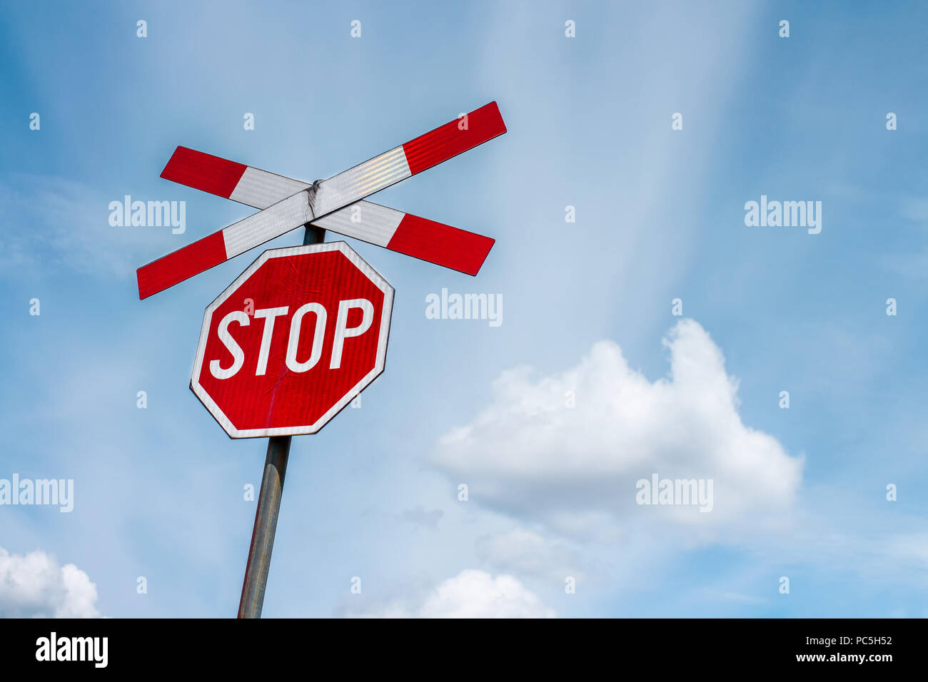 Red stop sign with railway cross sign and blue sky with white clouds in ...