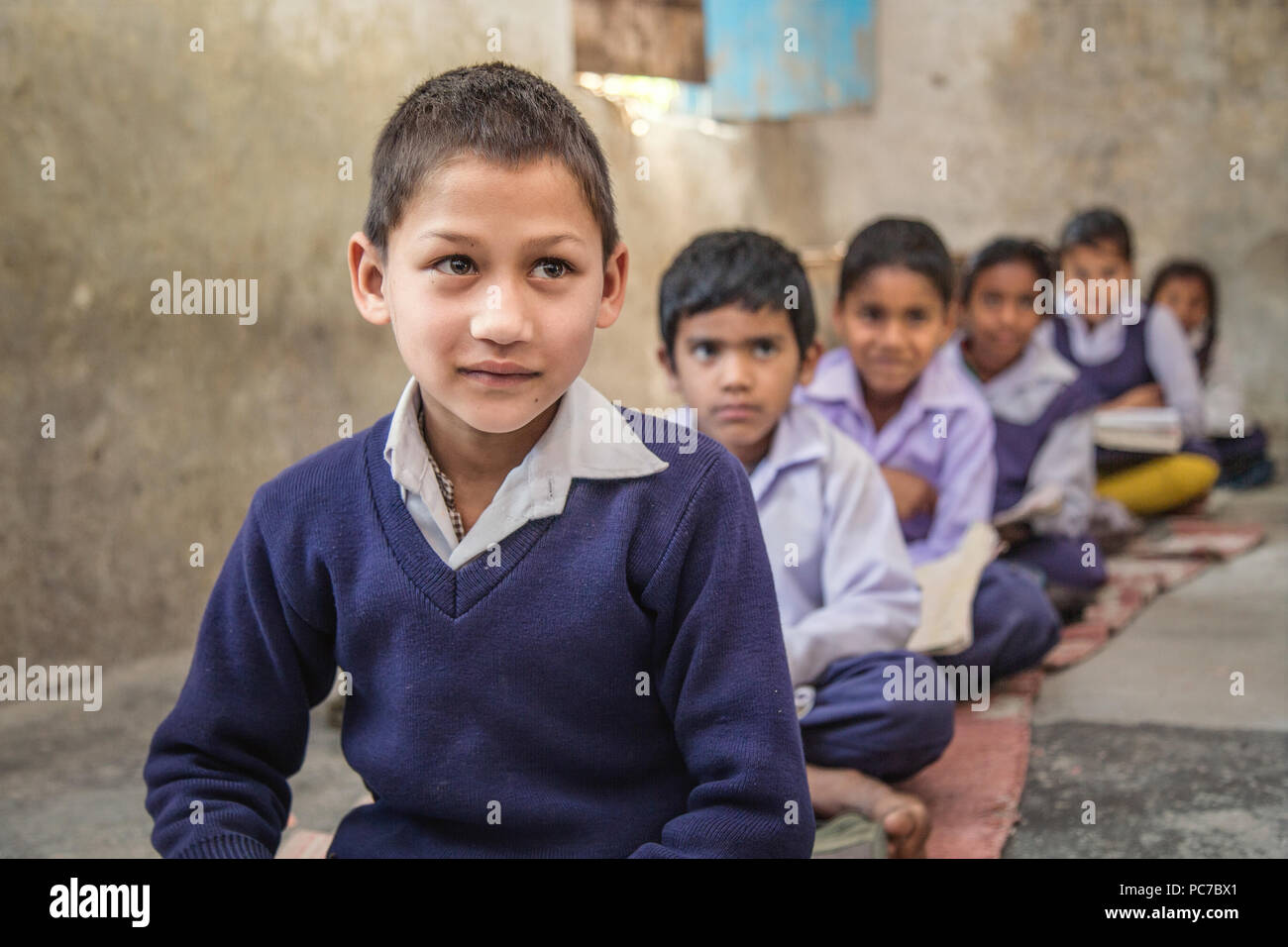 Village school boy portrait in school uniform, sitting on the floor of ...