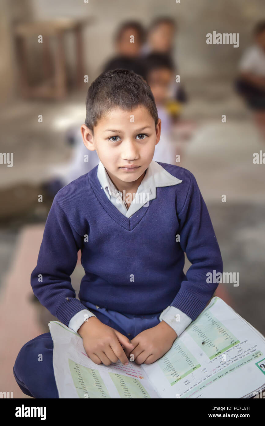 Village school boy portrait in school uniform, sitting on the floor of ...
