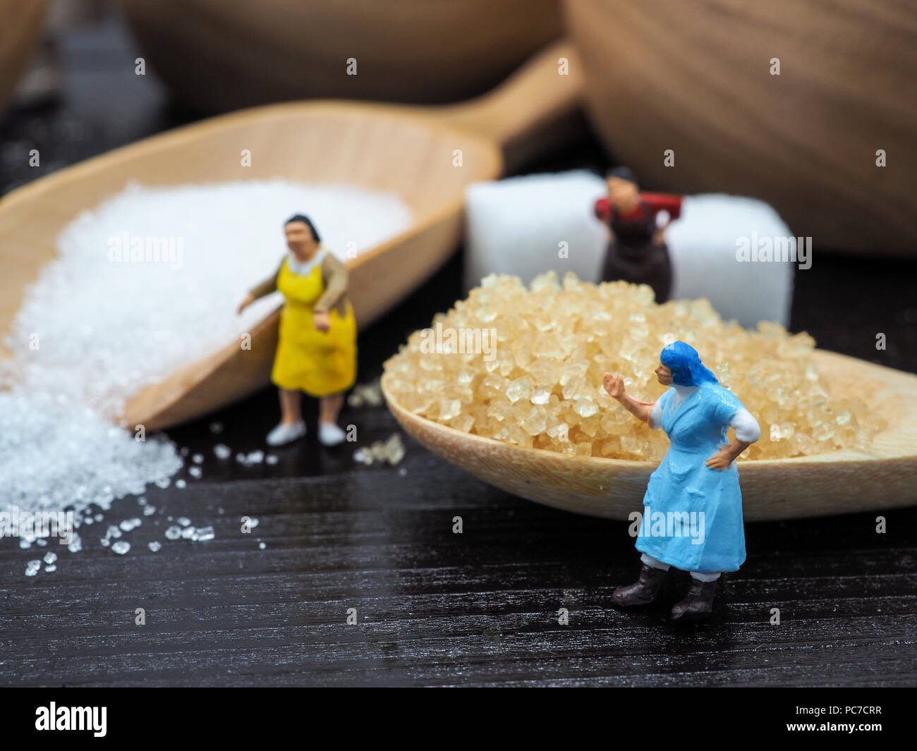 Miniature fat woman standing near wooden bowl and spoon with sugar cube ...
