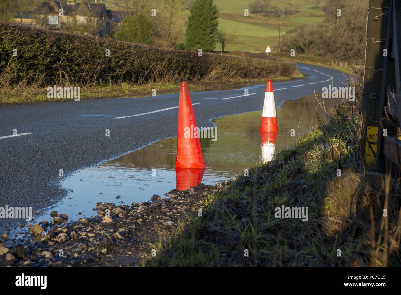Traffic cones indicating hidden potholes in a puddle on a country road ...