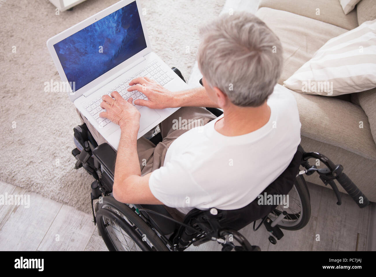 Man in wheelchair typing on laptop. Top view of elderly disabled man ...
