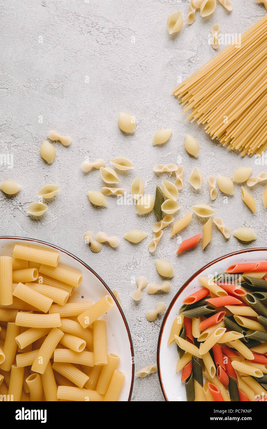 top view of different raw pasta in bowls on messy concrete tabletop ...