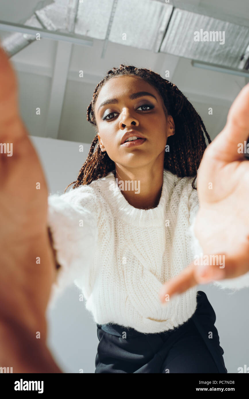 low angle view of beautiful stylish african american girl taking selfie and looking at camera ...