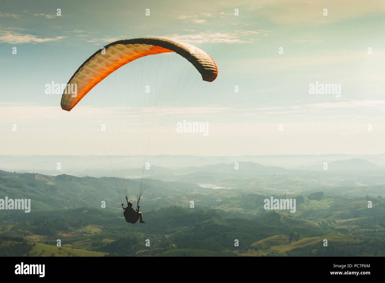 Paraglider flying on the beautiful sunny sky over the green mountains ...