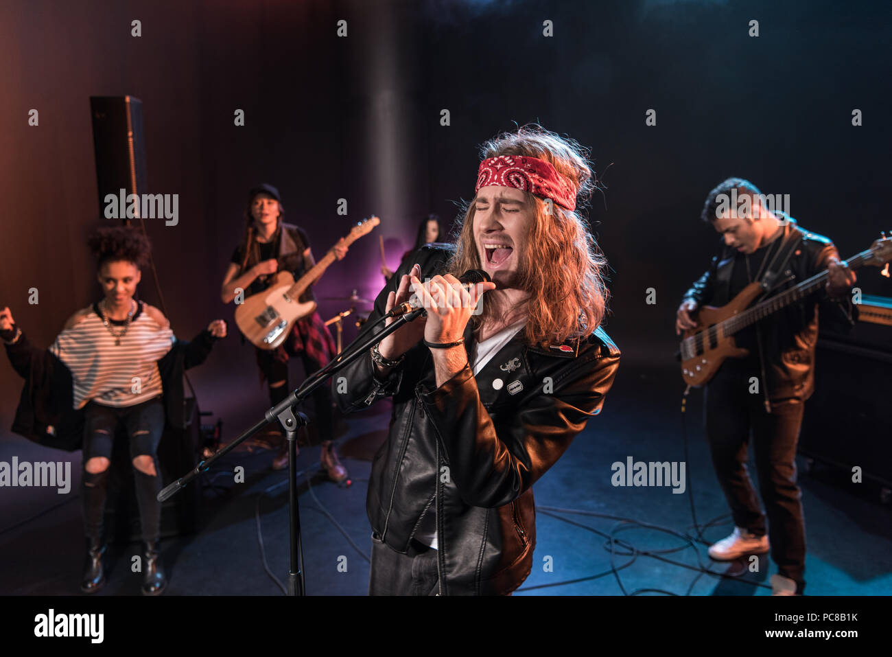 Handsome young singer with rock and roll band performing rock concert ...