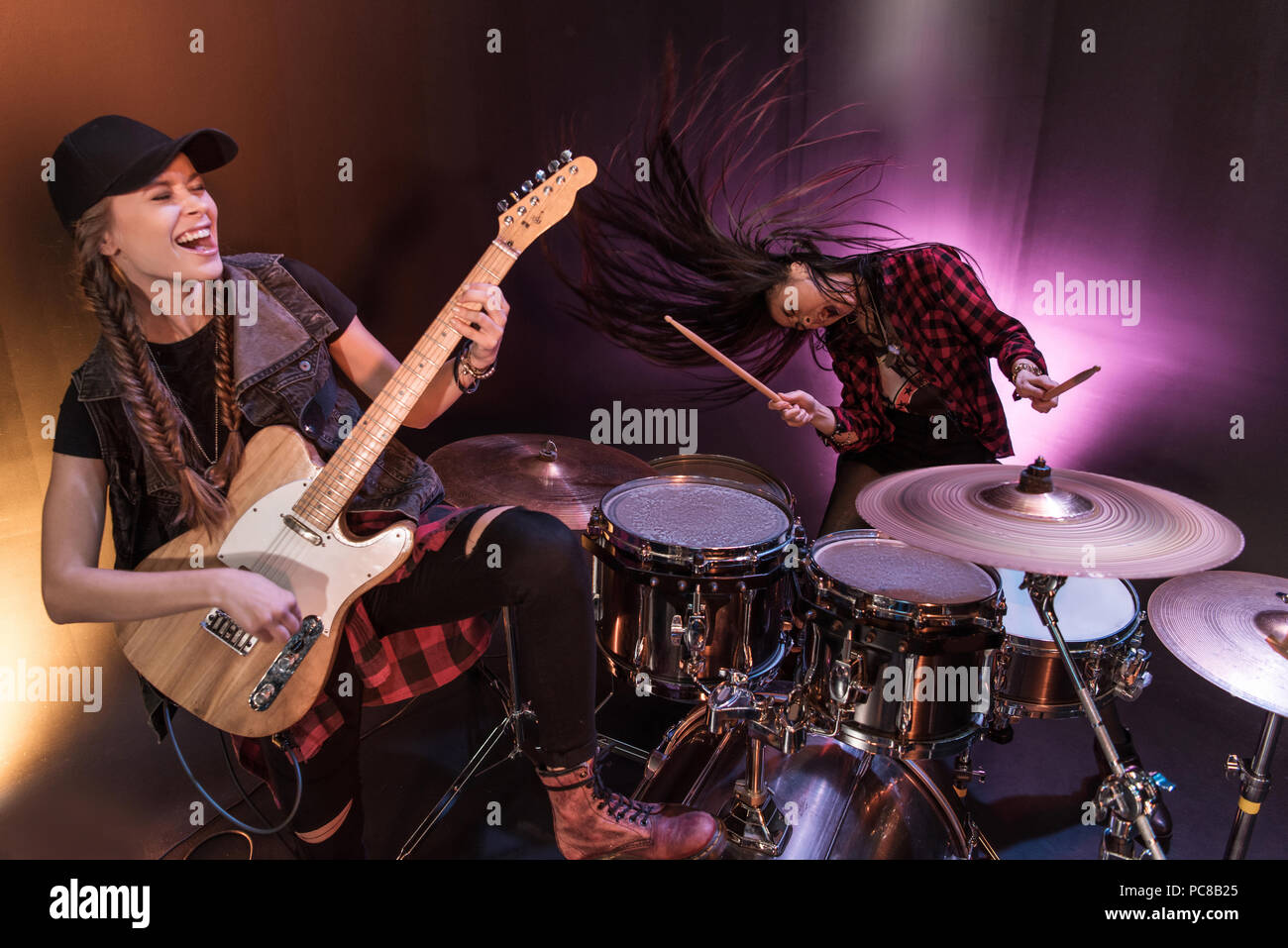 Excited young women with drums set and electric guitar performing rock ...