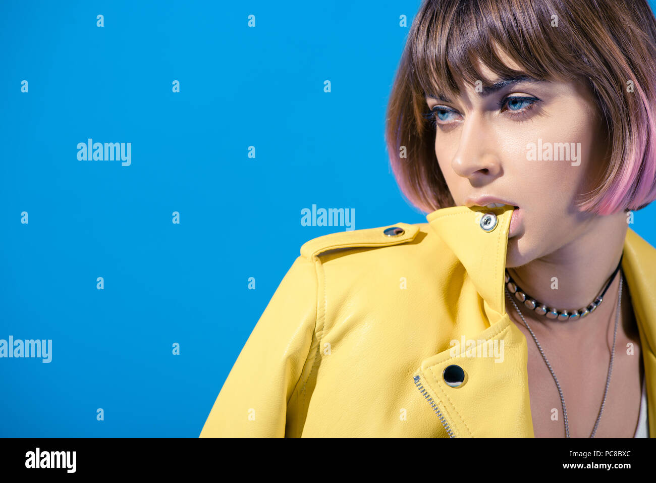 portrait of stylish girl biting leather jacket and looking away ...