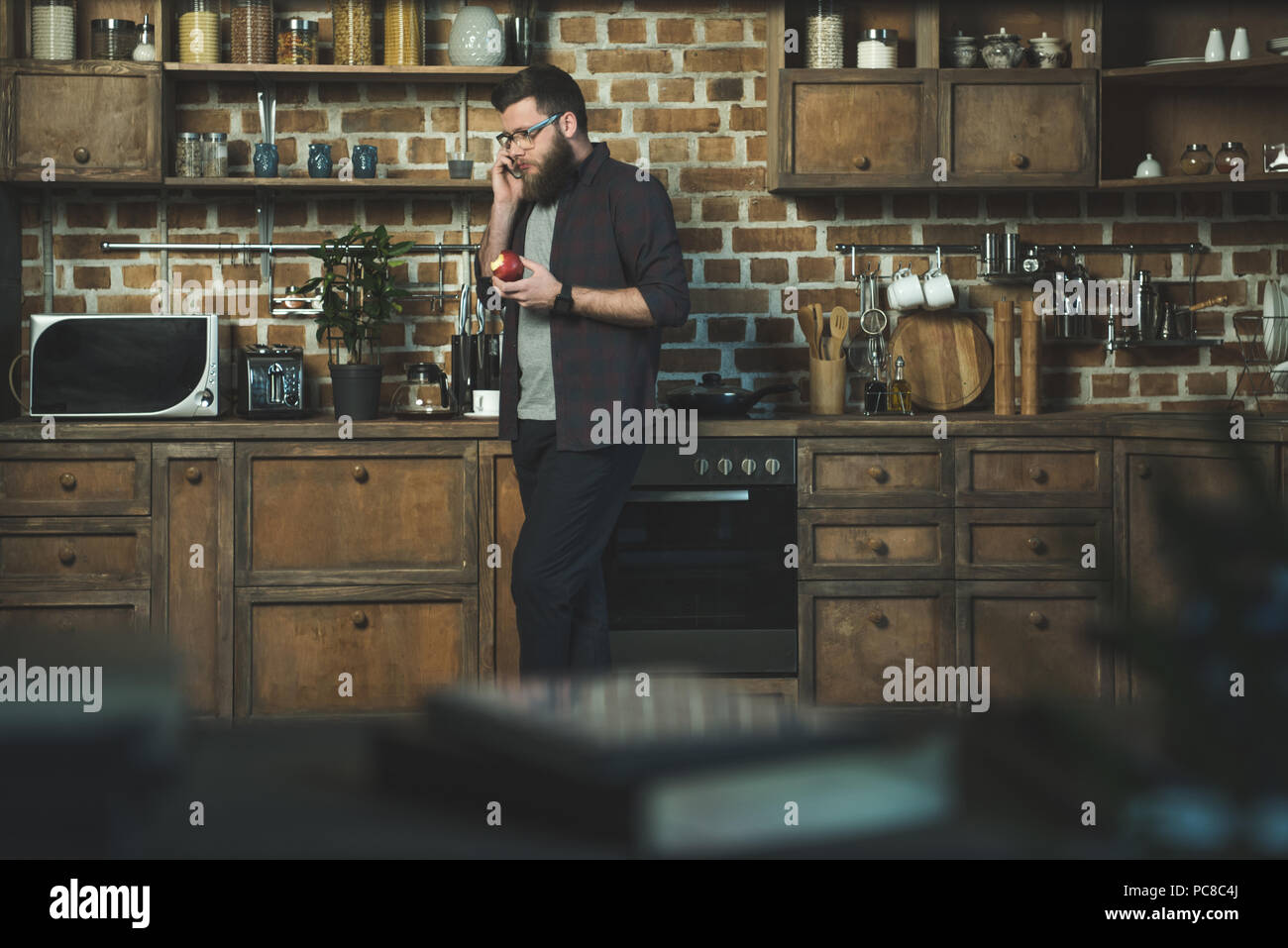 serious man talking on smartphone and eating apple at home Stock Photo ...