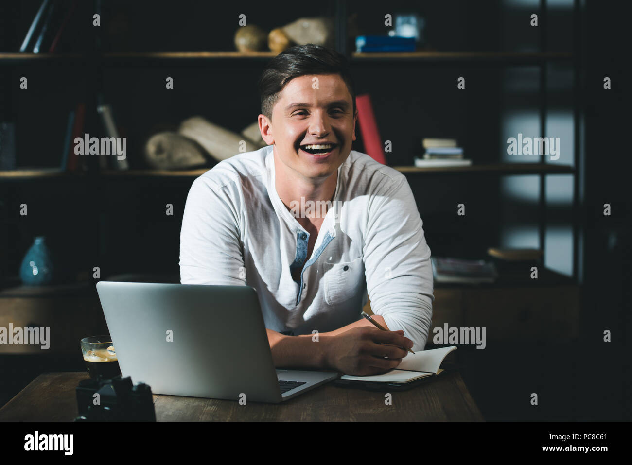 Stylish man in good mood taking notes during work at modern workplace ...