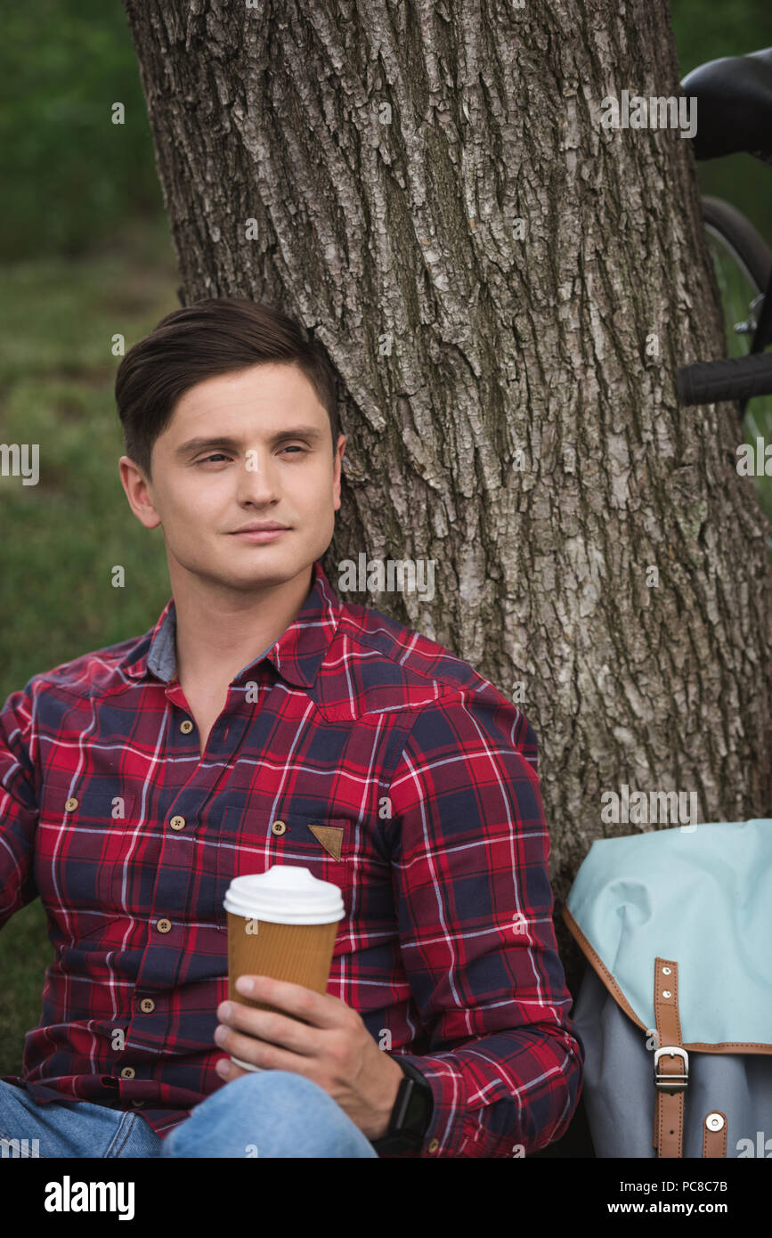 Man leaning to tree trunk and drinking coffee in disposable cup Stock ...