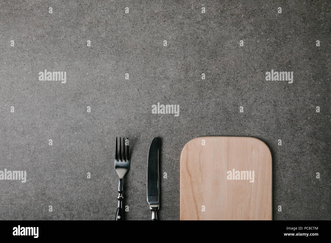 top view of wooden board with fork and knife on grey background Stock ...
