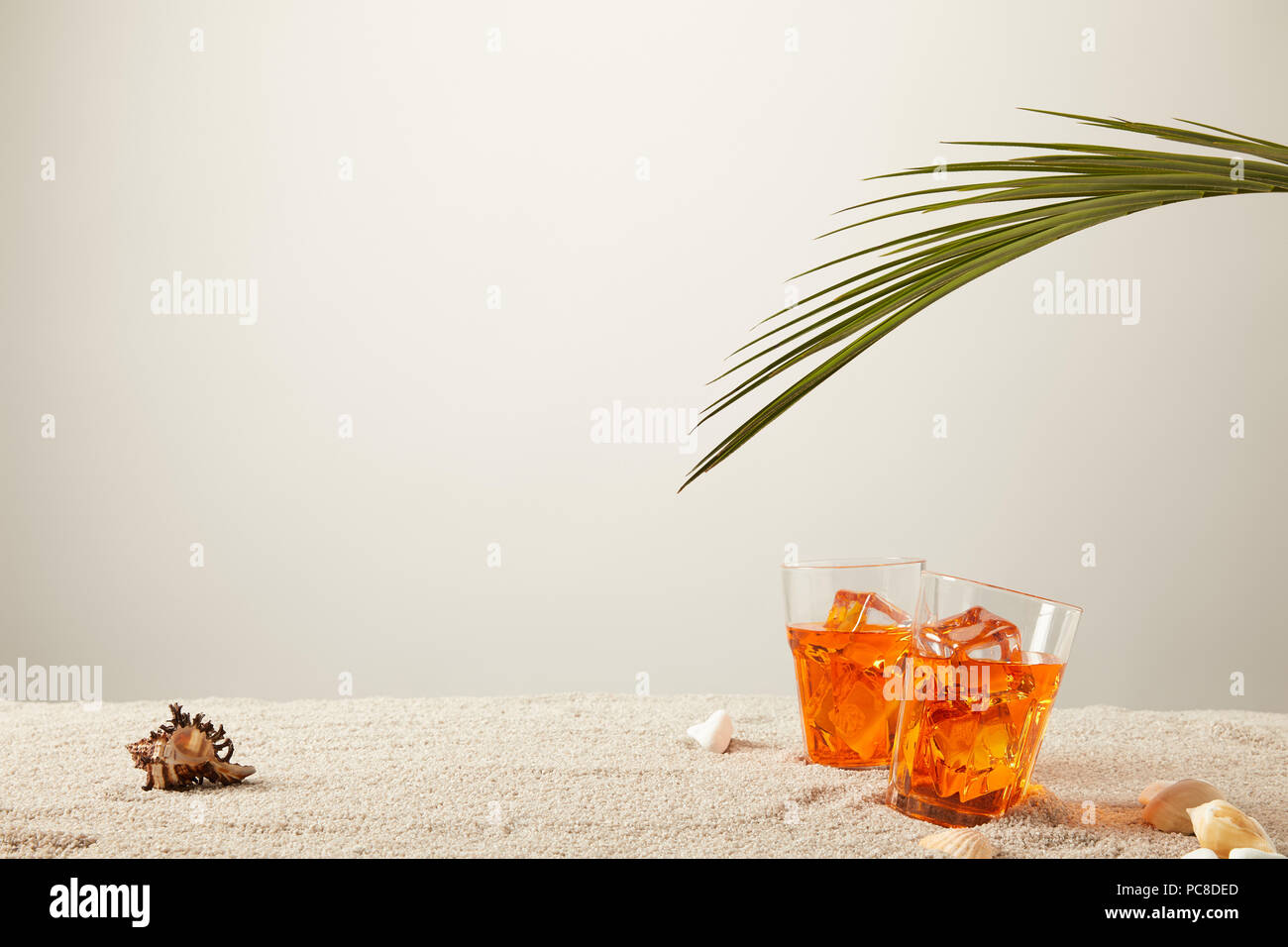 close up view of cocktails with ice with fern and seashells on sand on ... close up view of cocktails with ice with fern and seashells on sand on ...