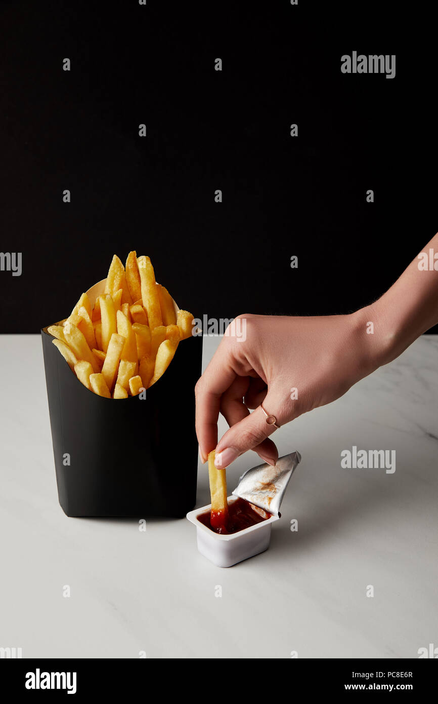 cropped shot of woman pouring french fry into ketchup isolated on black ...