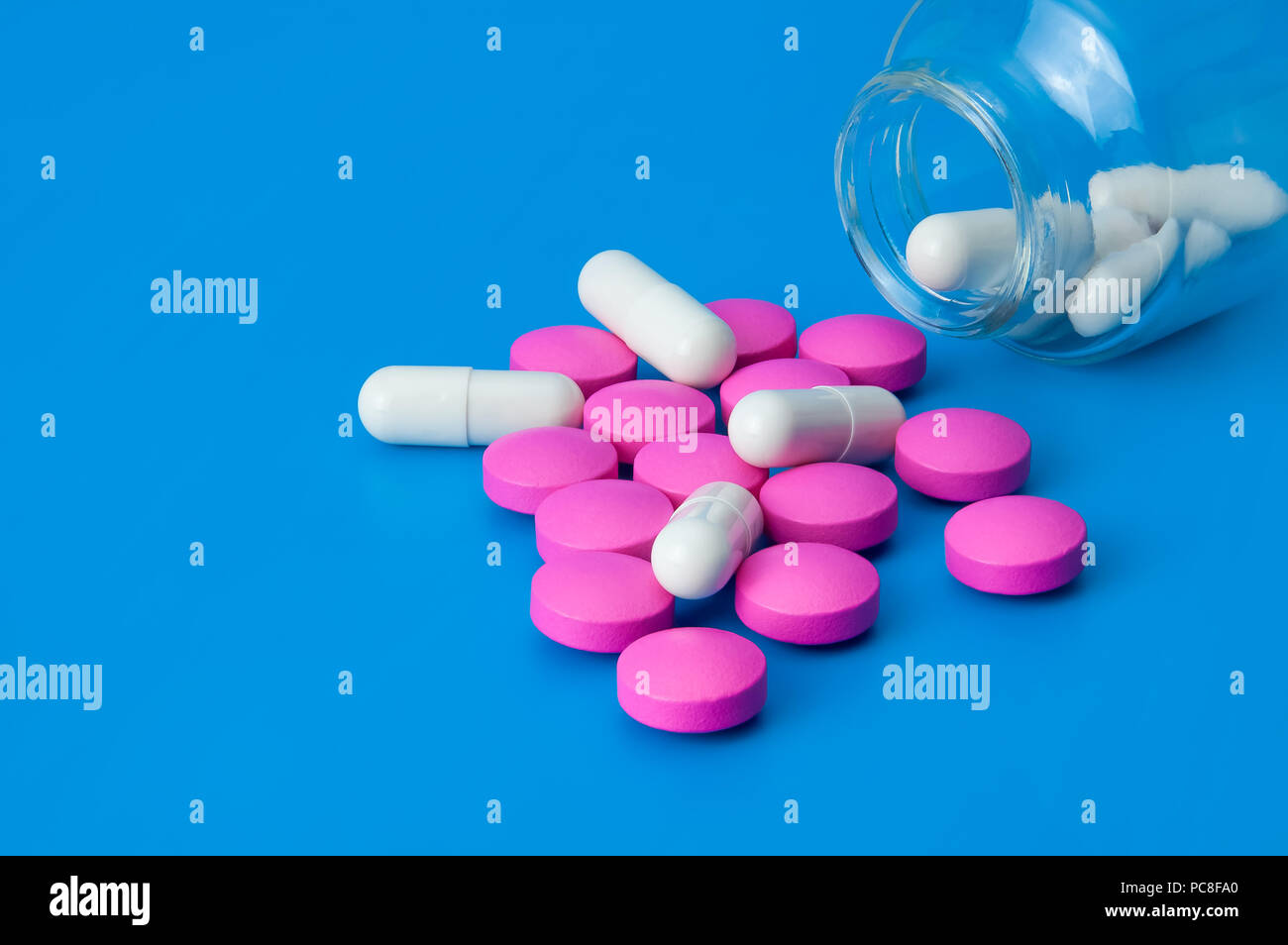 Large and bright red and white pills are scattered from a glass jar ...