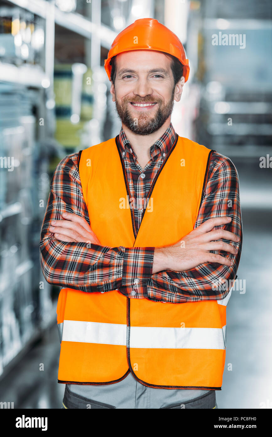 cheerful worker in helmet and safety vest with crossed arms in ...