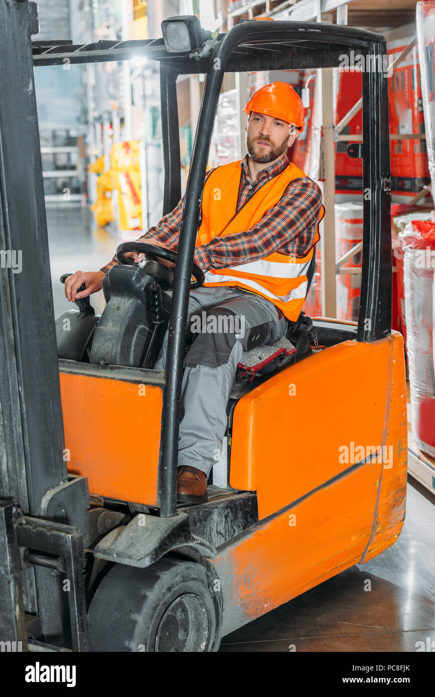 male worker in safety vest and helmet sitting in forklift machine in ...