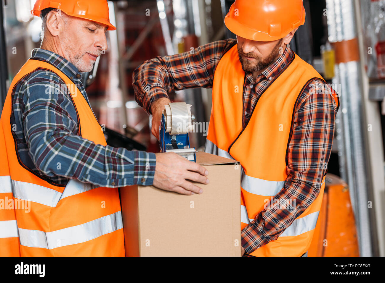 male workers in safety vests and helmets packing cardboard box with ...