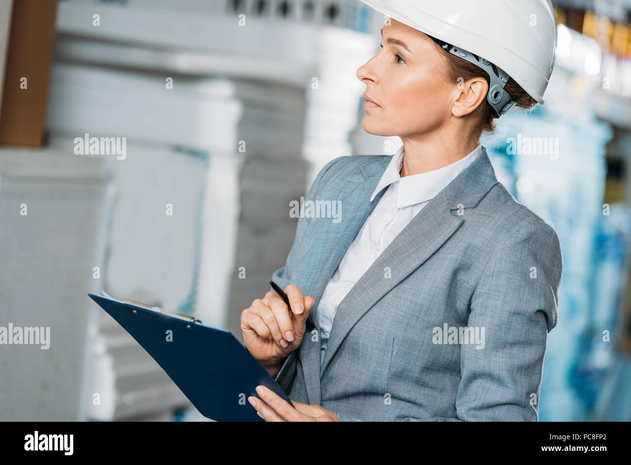 female inspector in helmet writing notes on clipboard in warehouse ...