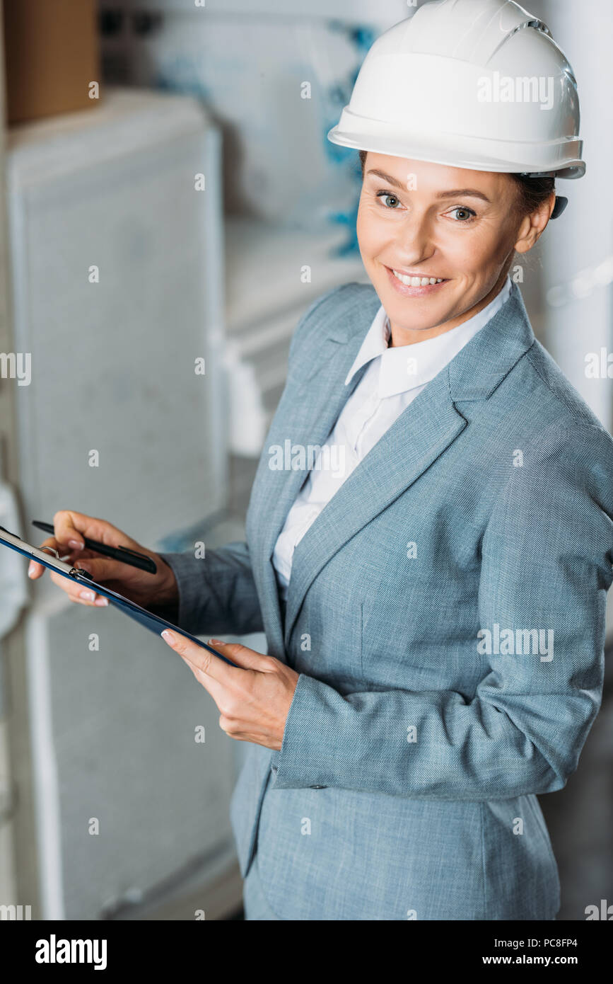 female inspector in helmet writing notes on clipboard in warehouse ...