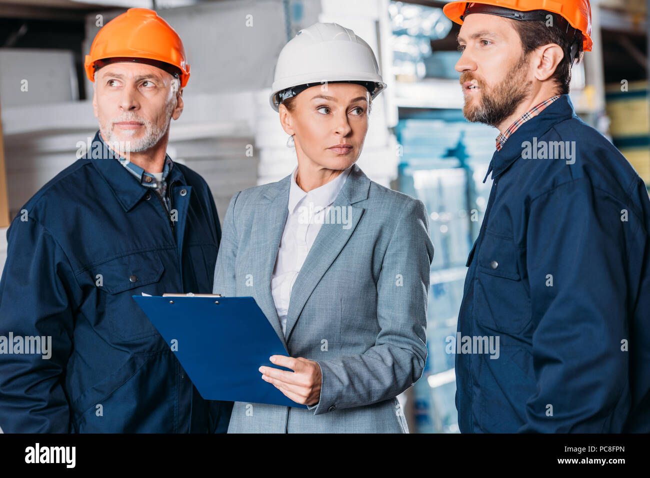 male workers in helmets and female inspector with clipboard in ...