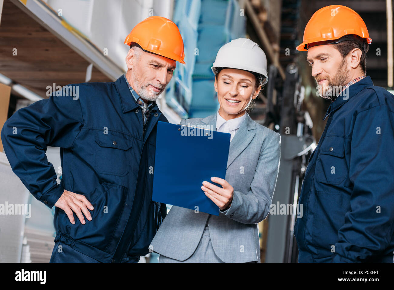 male workers and female inspector in helmets in warehouse Stock Photo ...
