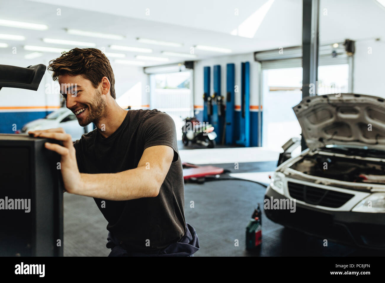 Smiling mechanic checking a car with computer in service station ...