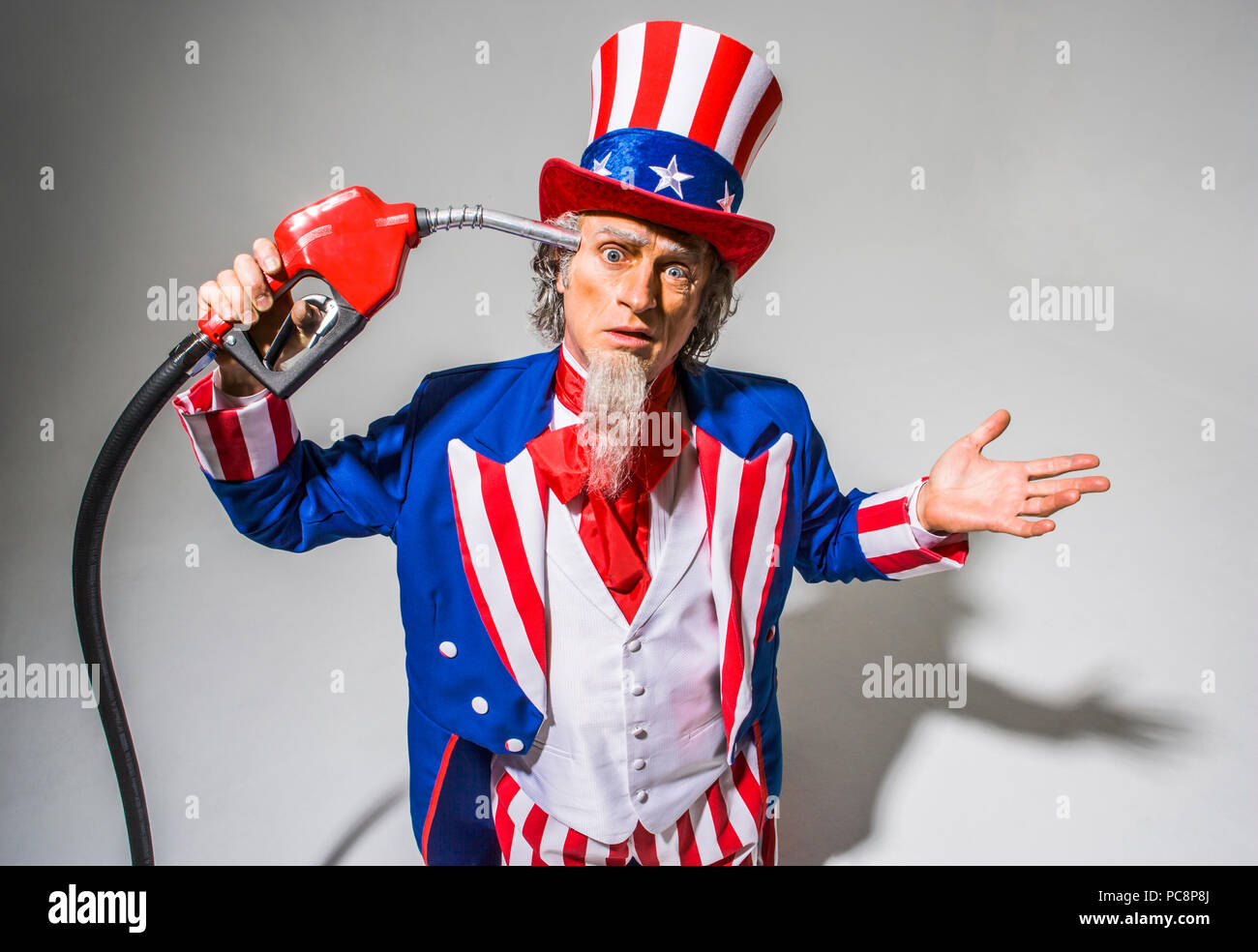 Uncle Sam standing with a gas pump nozzel held in front of him. Conceptual shot depicting the ...