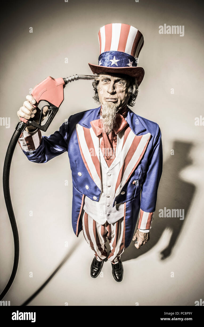 Uncle Sam standing with a gas pump nozzel held in front of him. Conceptual shot depicting the ...