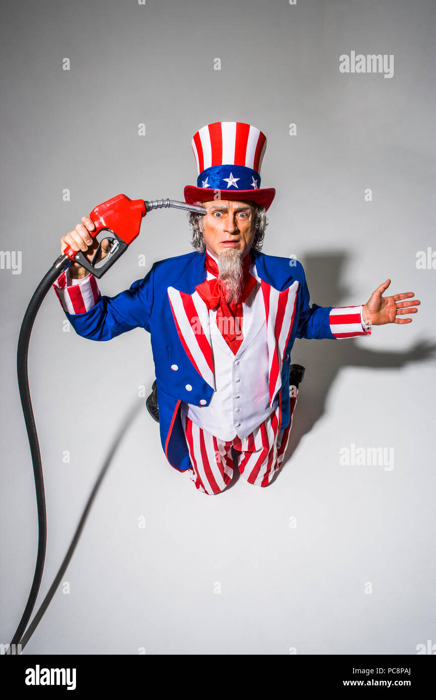 Uncle Sam standing with a gas pump nozzel held in front of him. Conceptual shot depicting the ...