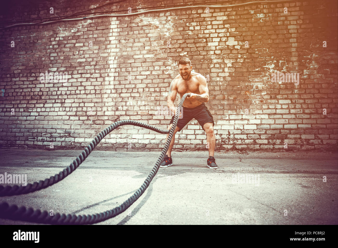 Athletic man working out with rope in front of brick wall. Strength and ...